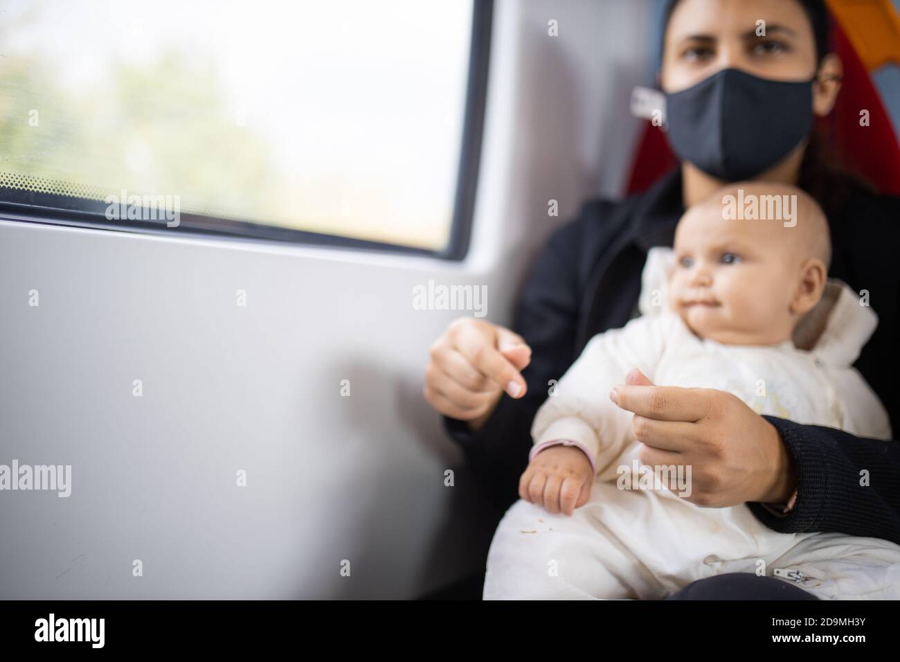 Baby resting on the legs of her mother and looking through the window ...