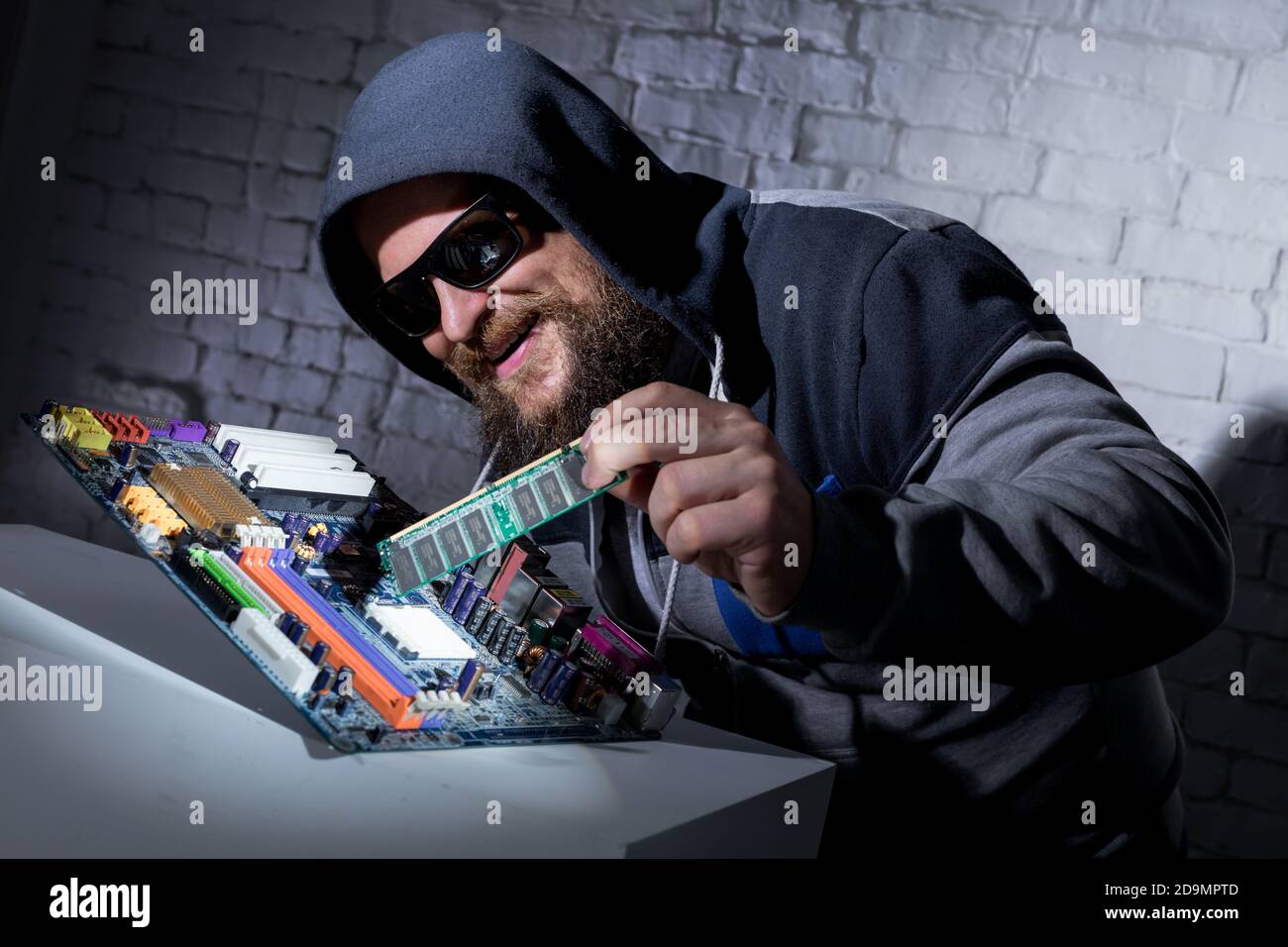 Bearded hacker in sunglasses and hoodie cracking the hardware studio ...