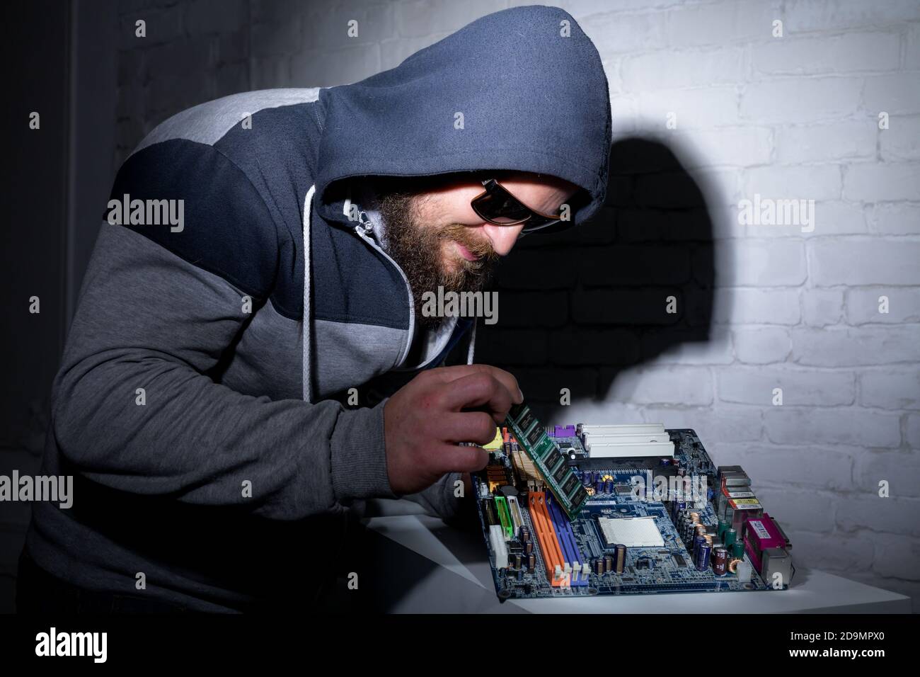Bearded hacker in sunglasses and hoodie cracking the hardware studio ...
