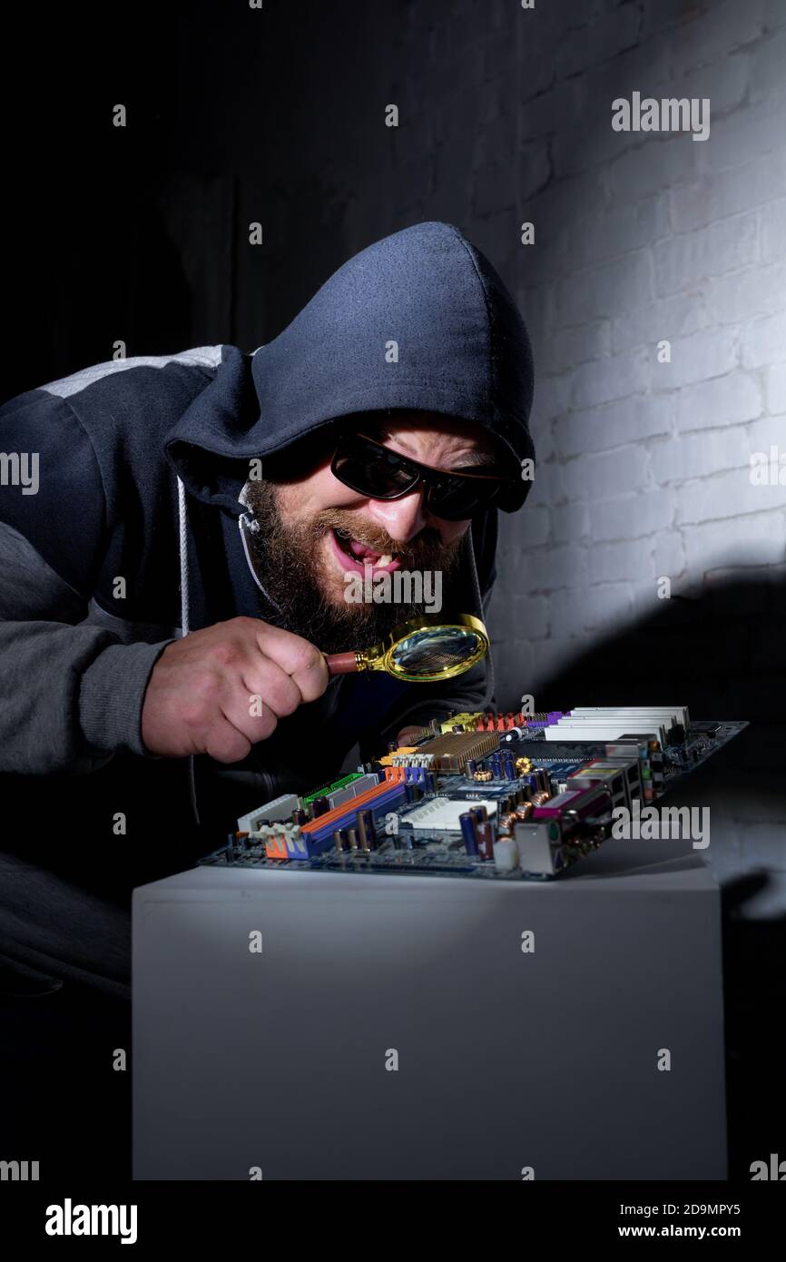 Bearded hacker in sunglasses and hoodie cracking the hardware studio ...