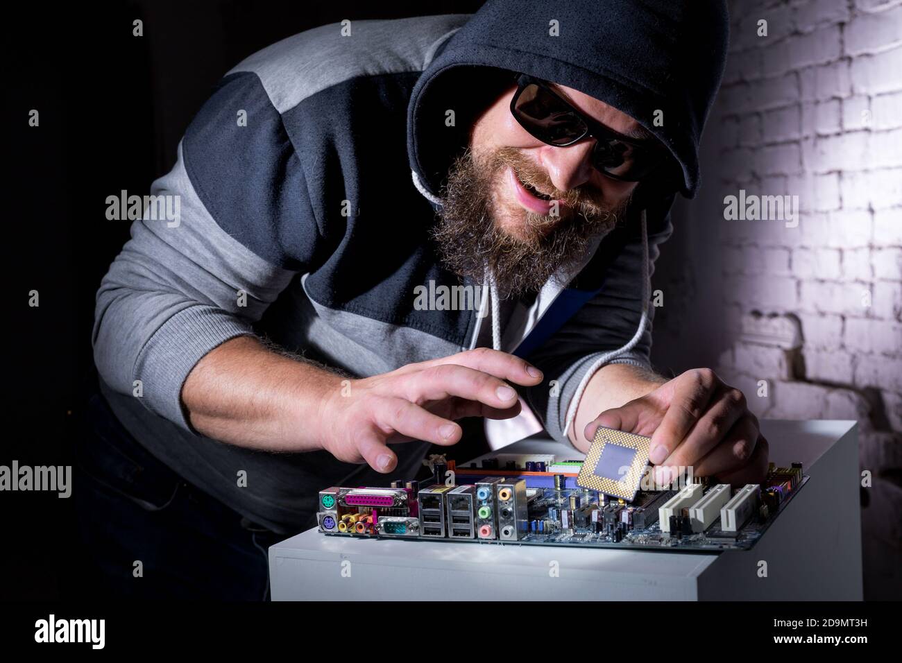 Bearded hacker in sunglasses and hoodie cracking the hardware studio ...