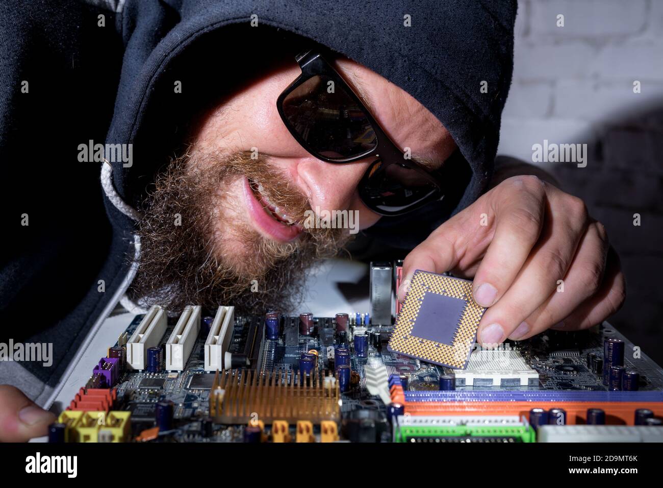 Bearded hacker in sunglasses and hoodie cracking the hardware studio ...
