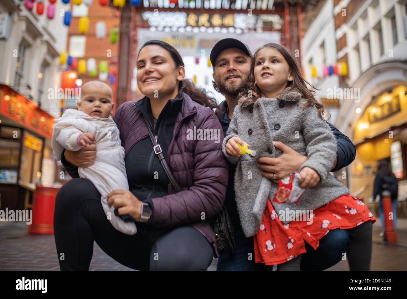 Two happy parents and their two daughters posing in a blurry Chinatown ...