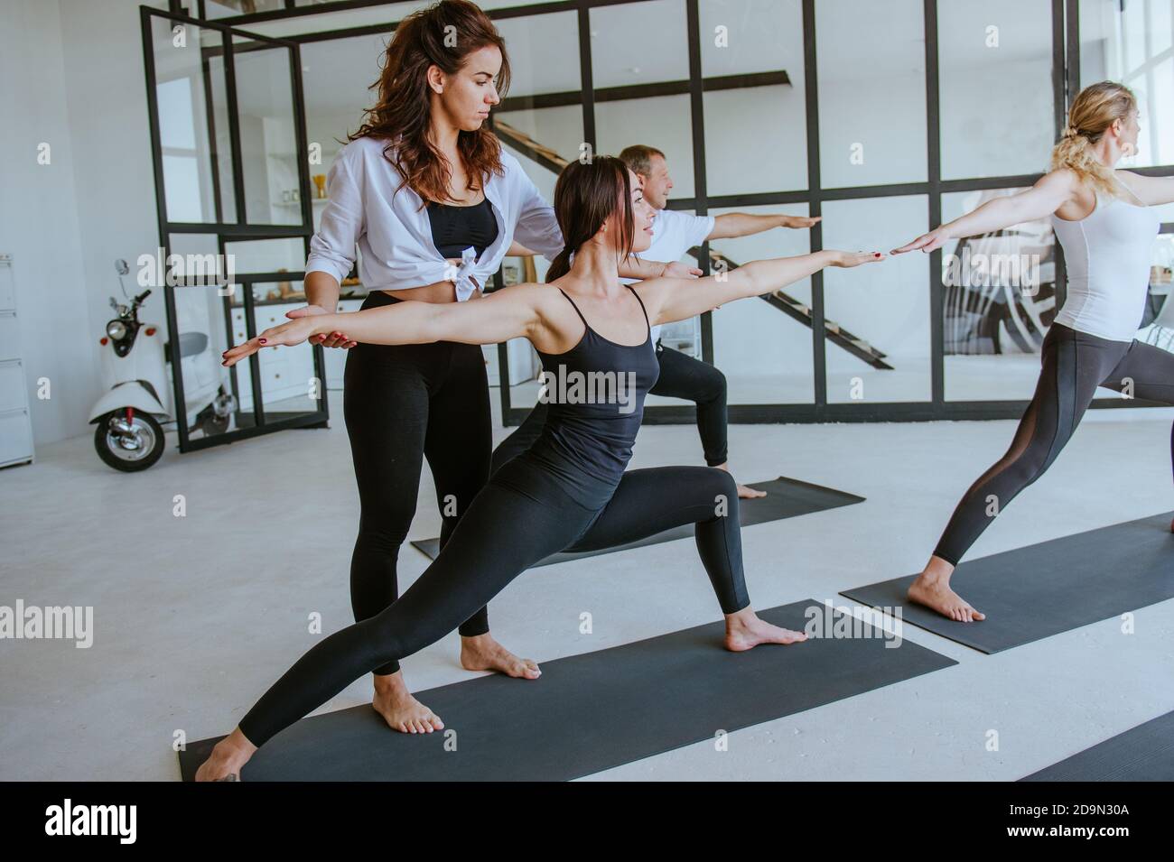 Yoga instructor helping young woman practicing yoga pose. Group yoga ...
