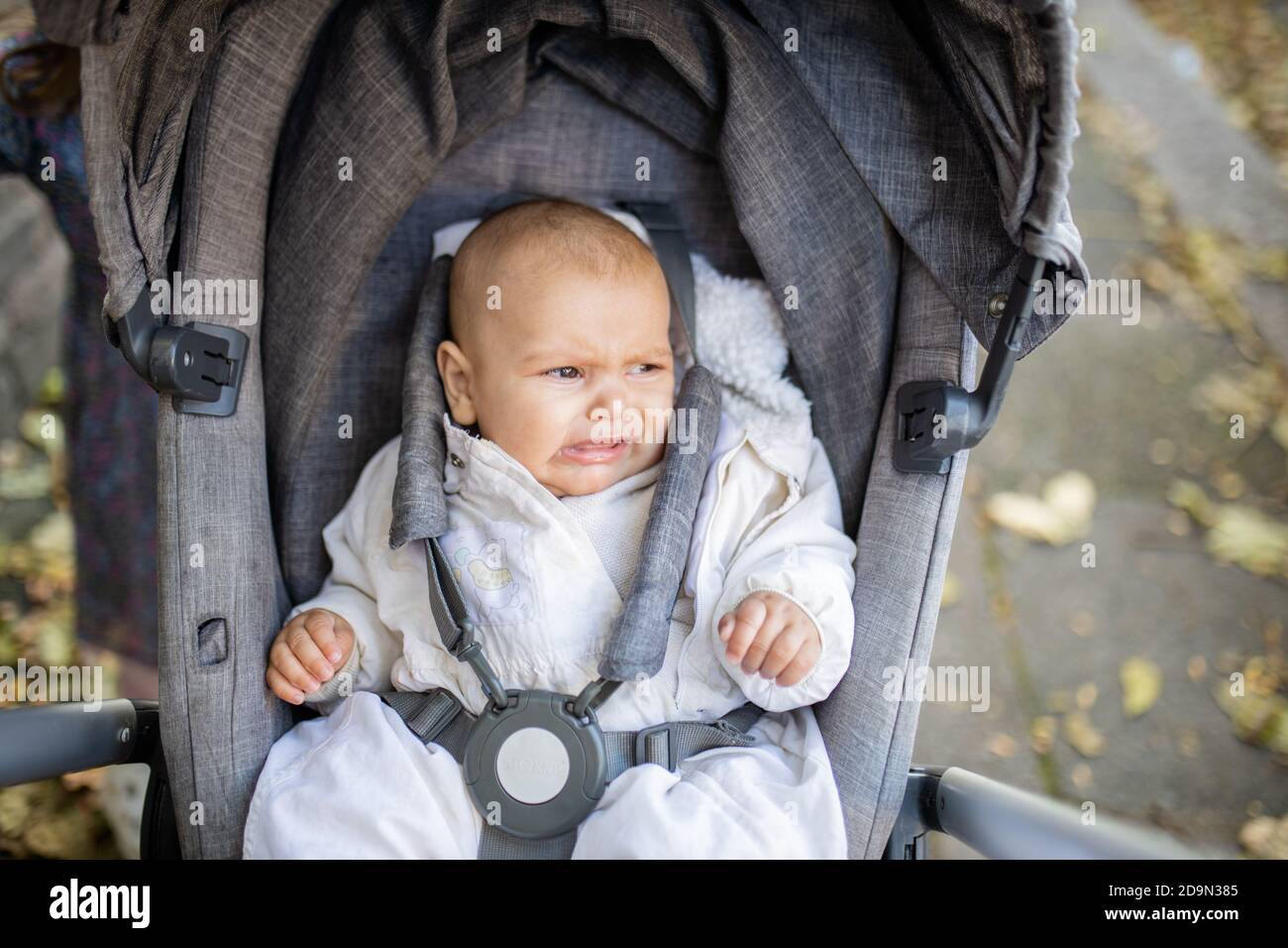 A distressed baby in a gray stroller looking at the distance and crying ...