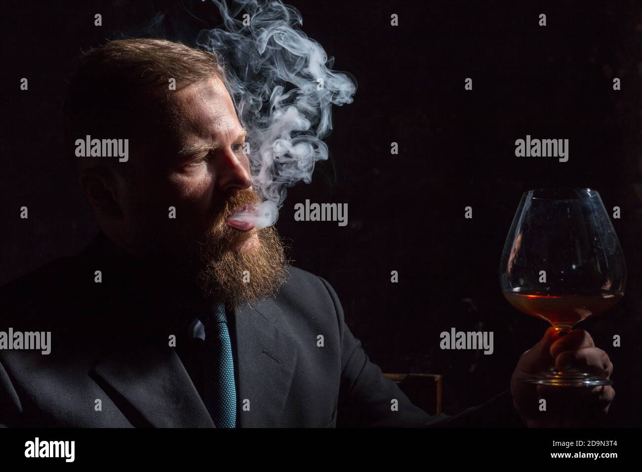 Solid confident bearded man in suit with glass of whisky and fume ...