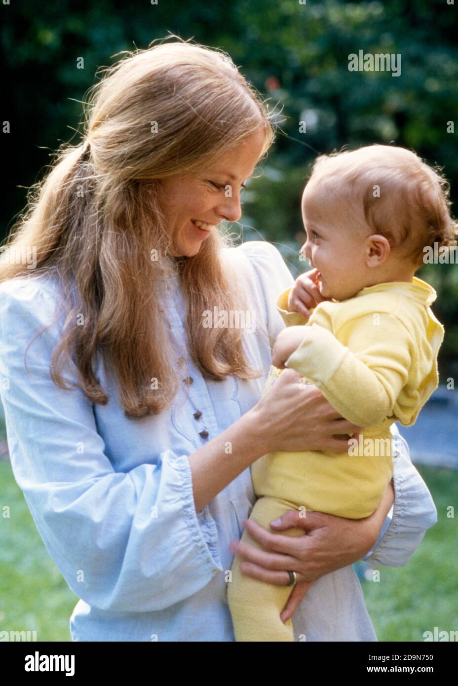 1970s BLONDE MOTHER WITH LONG HAIR HOLDING BABY IN YELLOW OUTFIT IN HER ...