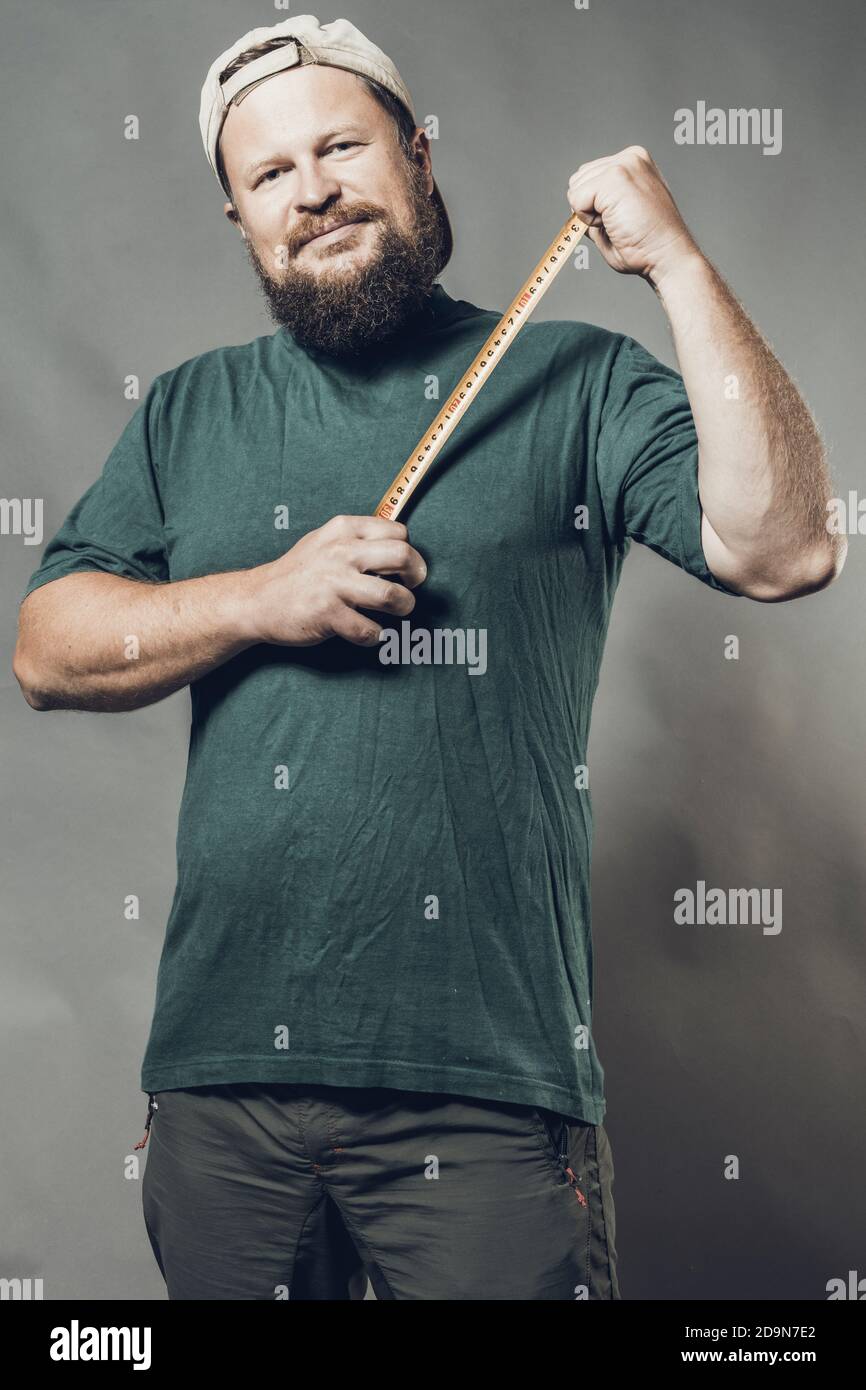 Joyful bearded craftsman in green t-shirt with tape measure studio ...