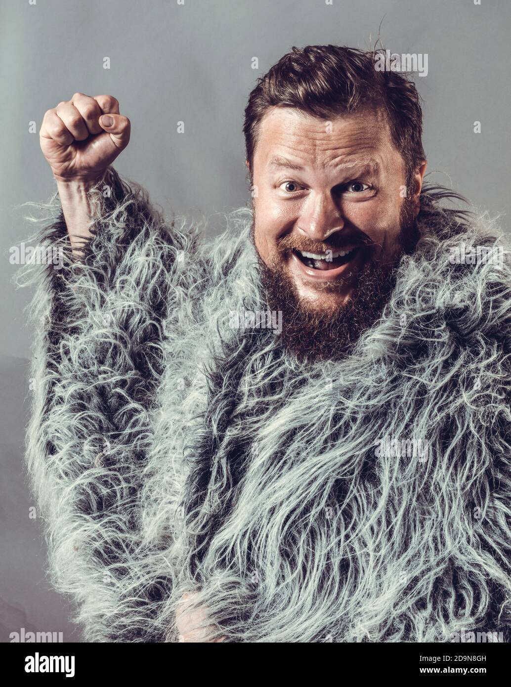 Solid bearded man in a fur mantle studio emotional portrait on grey ...