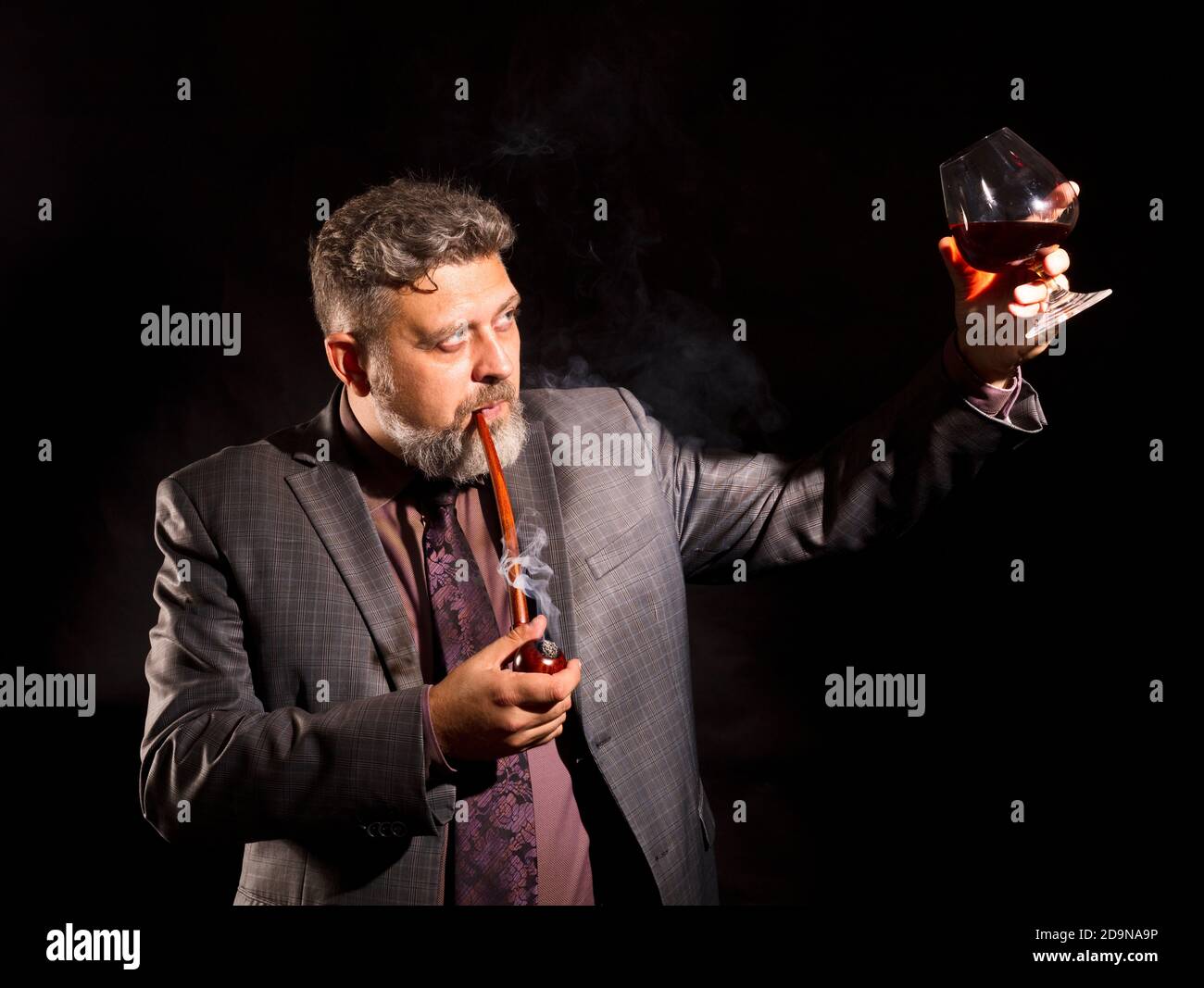 Solid confident bearded man in suit with glass of whisky smoking pipe ...