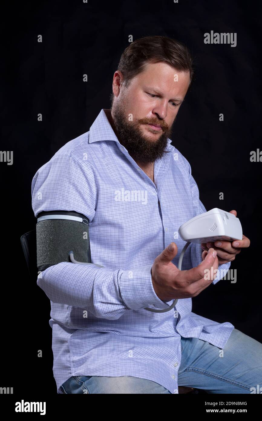 Preoccupied bearded man with tonometer measuring pressure to himself ...
