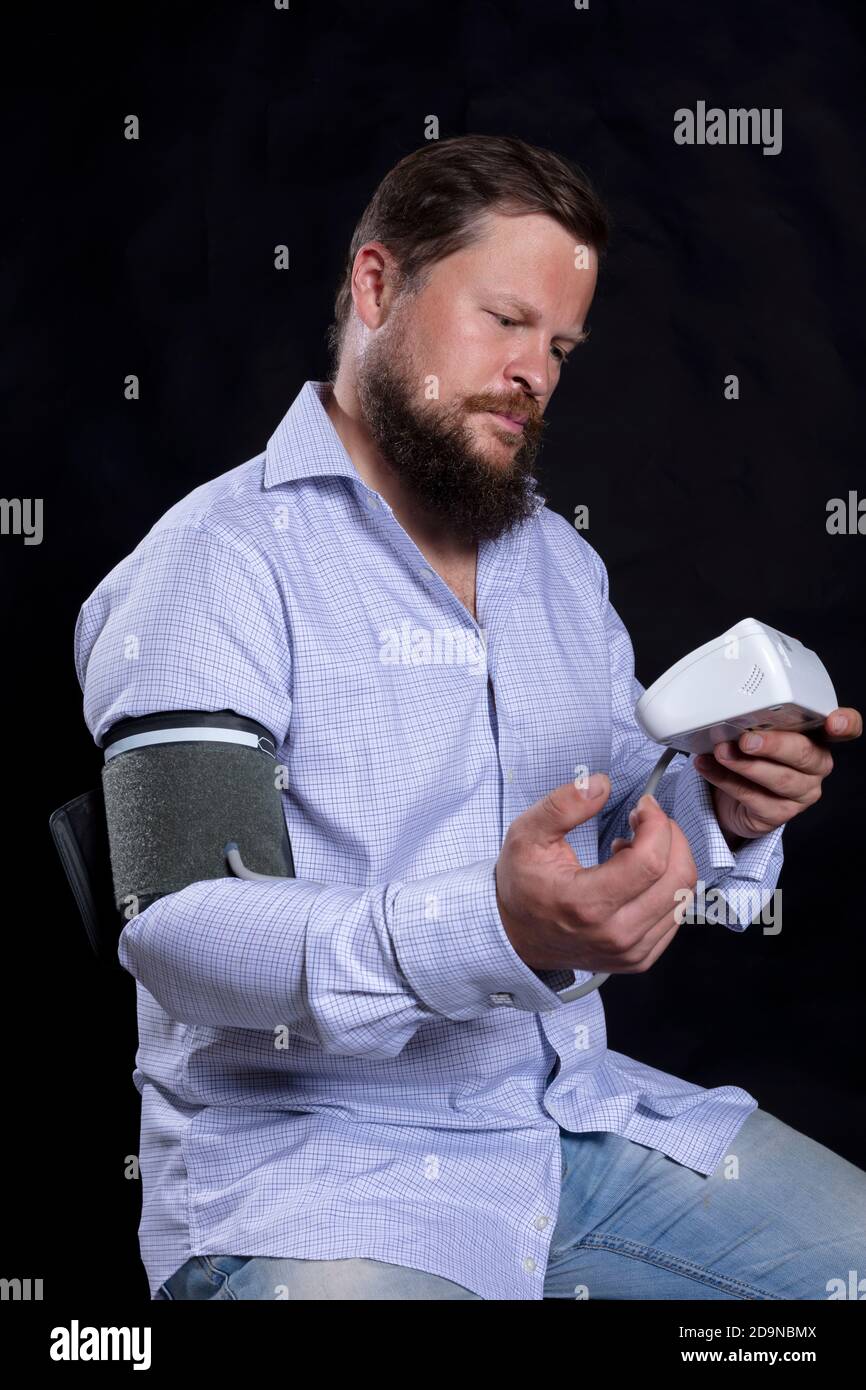 Preoccupied bearded man with tonometer measuring pressure to himself ...
