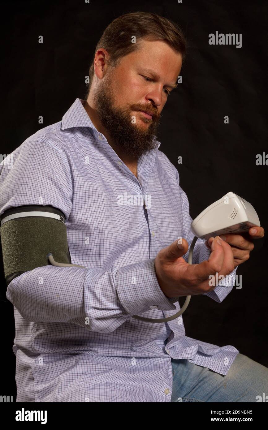 Preoccupied bearded man with tonometer measuring pressure to himself ...