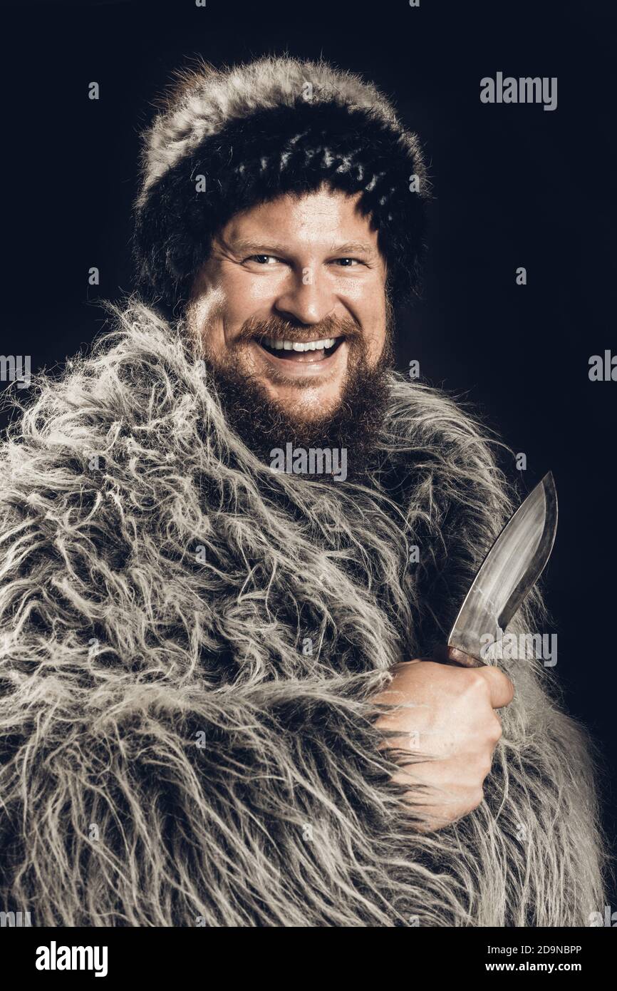 Bearded hunter dressed in a fur mantle and fur hat with knife studio ...