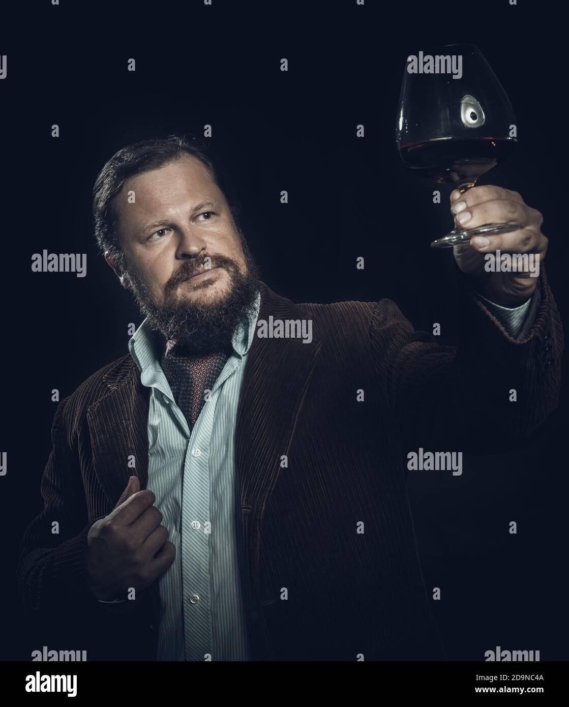 Stylish bearded man dressed in brown jacket with glass of whisky studio ...