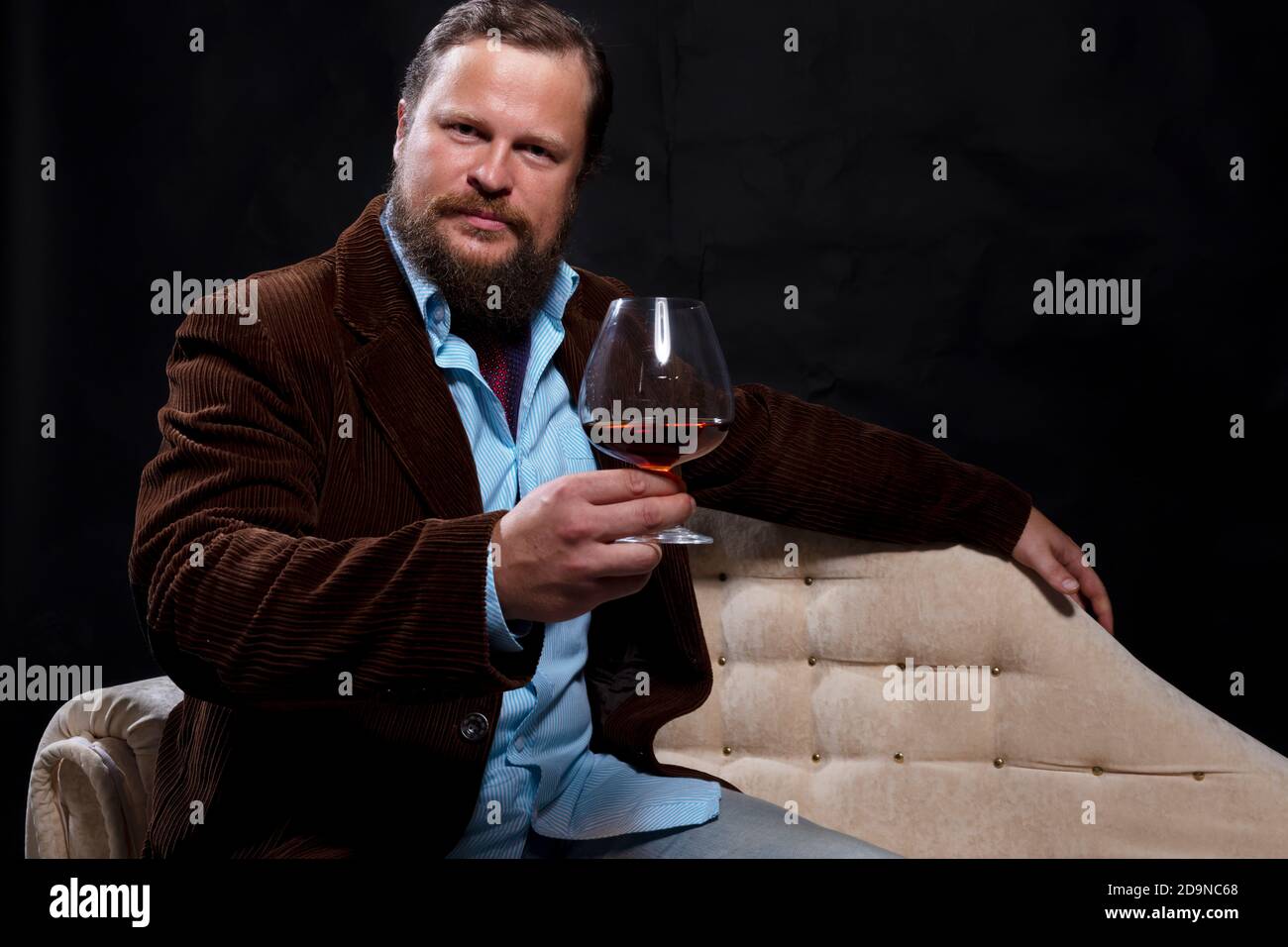 Stylish bearded man dressed in brown jacket with glass of whisky studio ...