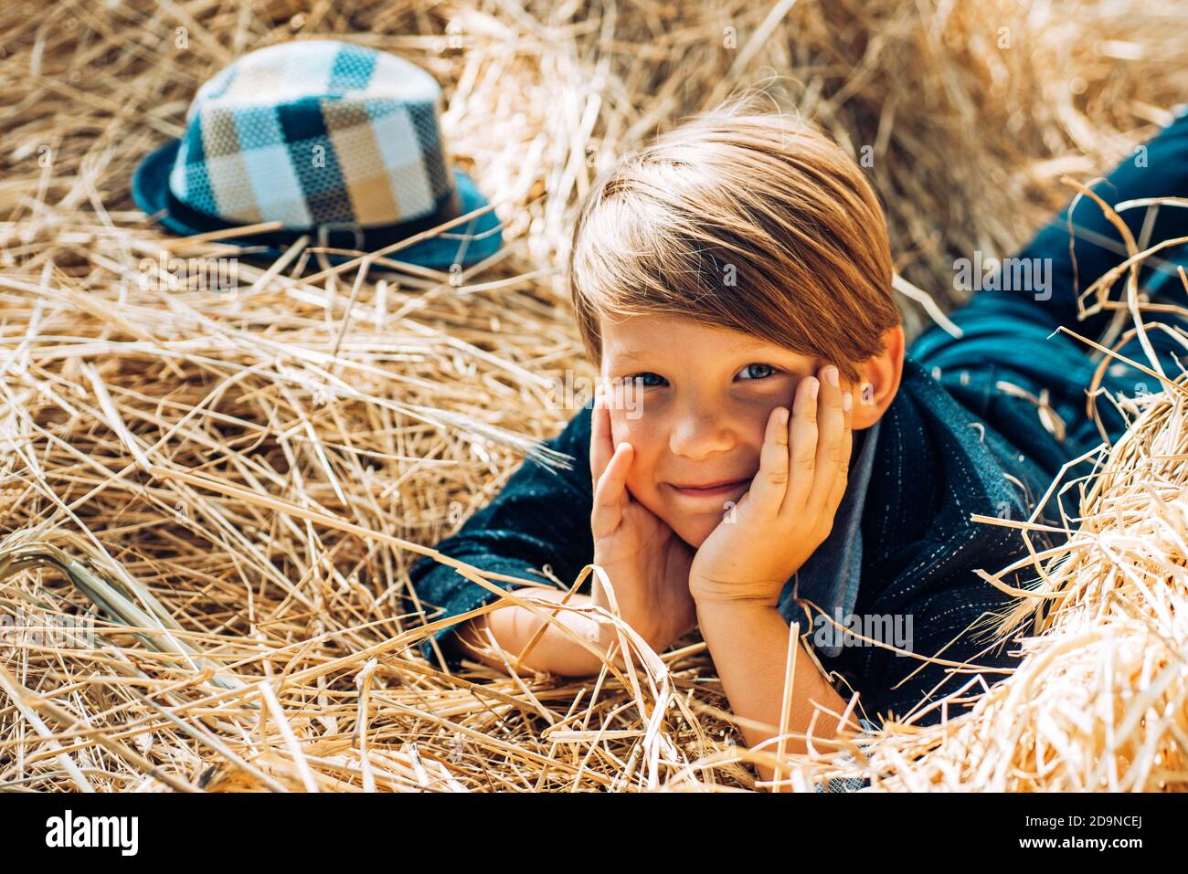 Kid boy lies on the hay. Cute little child boy holding gold leaf on ...