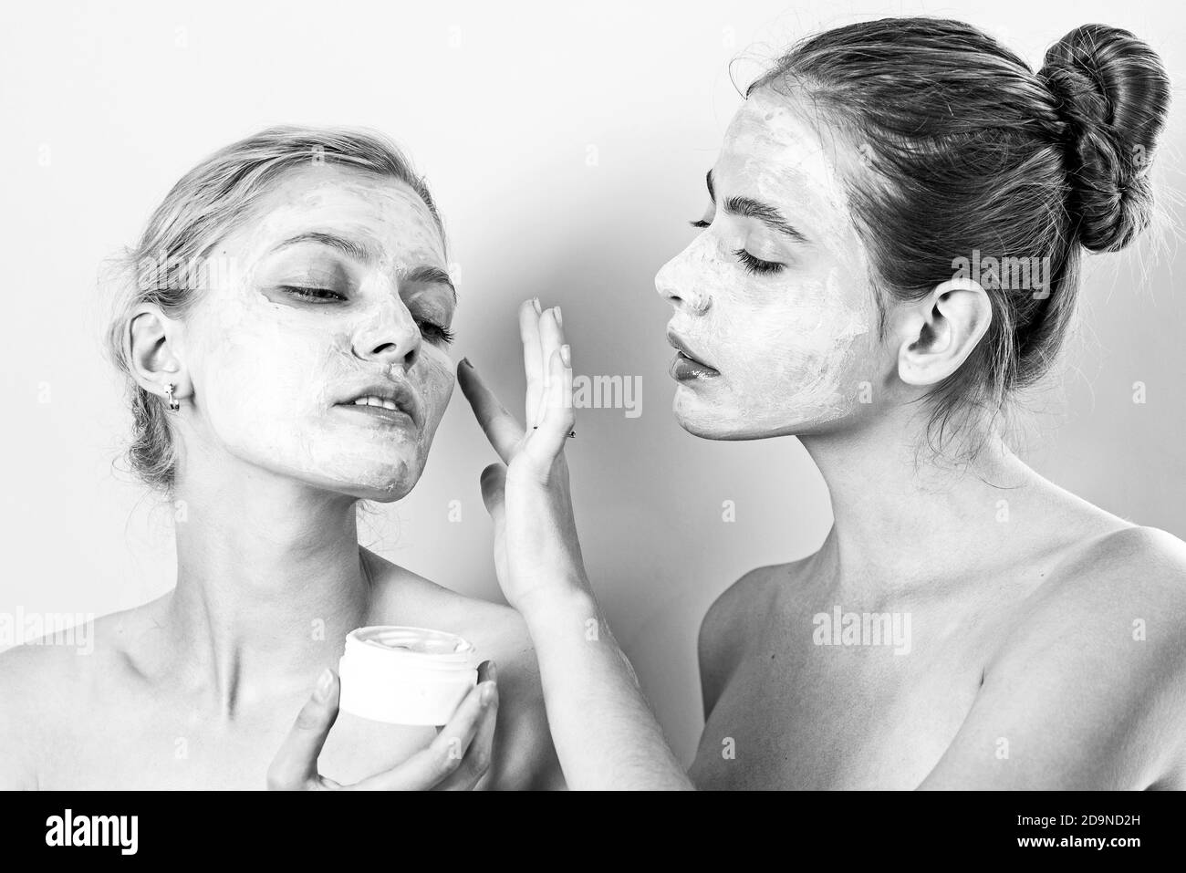 Two young women applying moisturizer cream on their face. Photo of ...