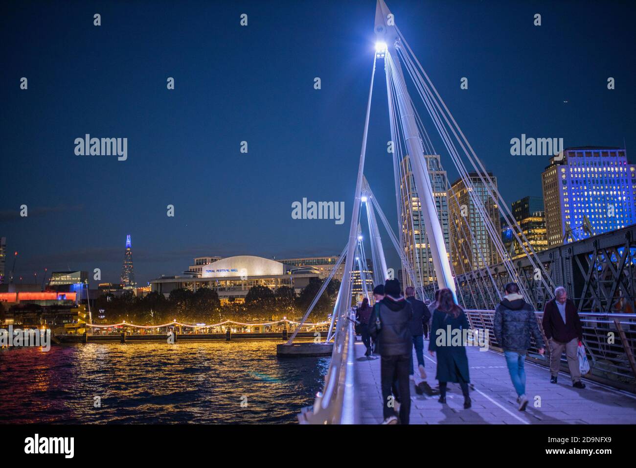 Cityscape at night from the handrail of a bridge with pedestrians ...