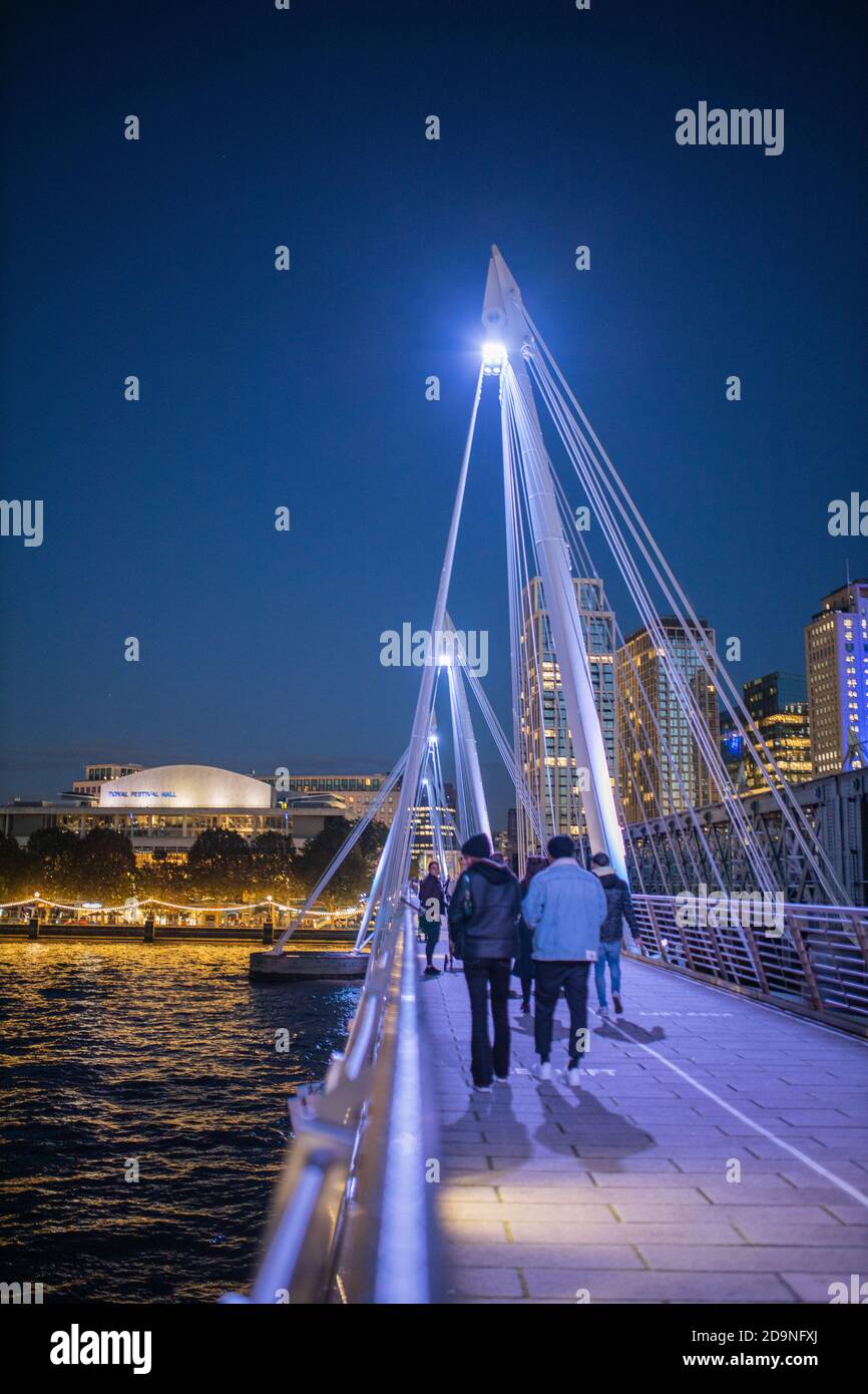Cityscape at night from the handrail of a bridge with pedestrians ...