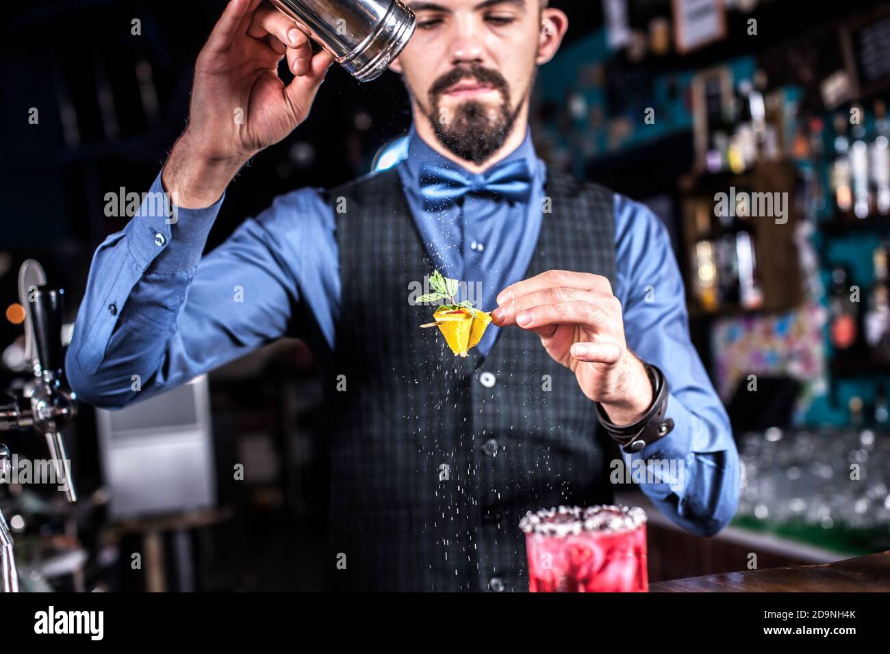 Expert bartender places the finishing touches on a drink while standing ...