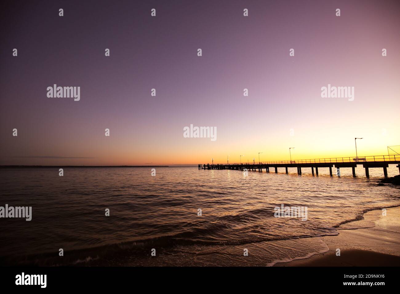 Mesmerizing view of a sunset over waves hitting the sand and a pier on ...