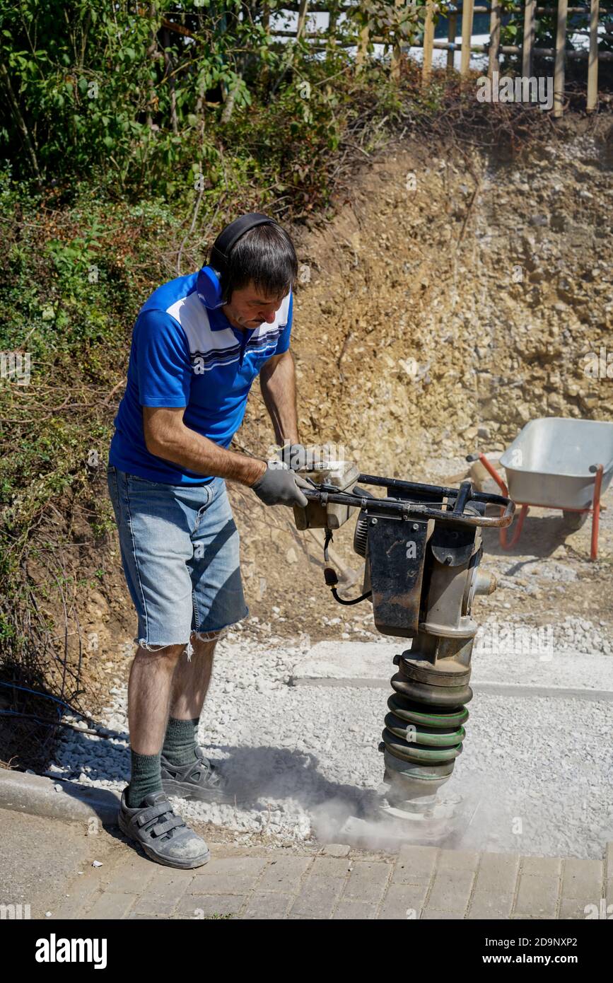 A Caucasian construction worker compacting soil using a tamping rammer ...
