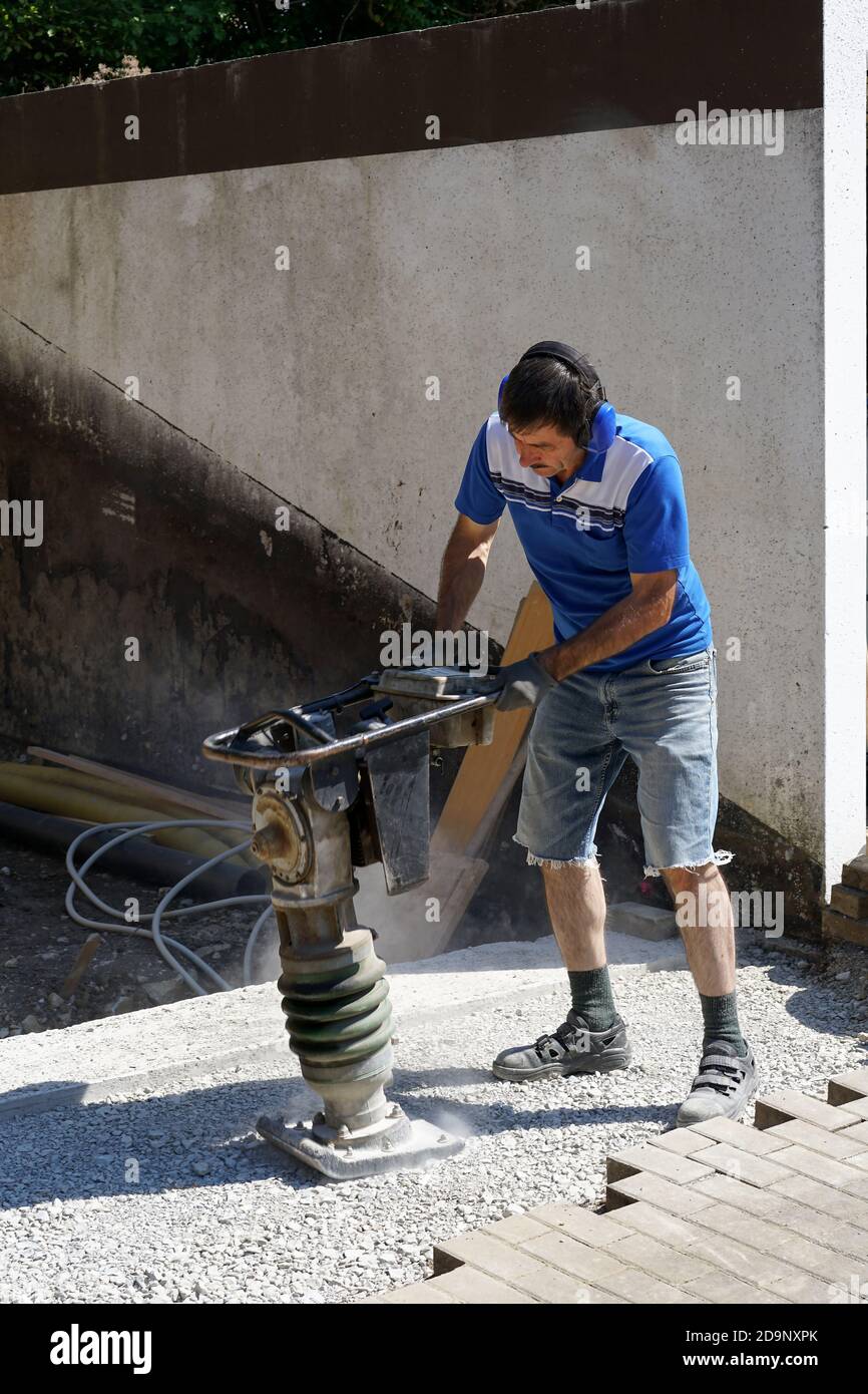 A Caucasian construction worker compacting soil using a tamping rammer ...