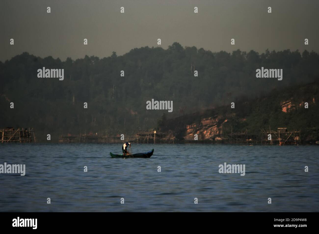A subsistence fisher working with a fishing net from a small wooden ...