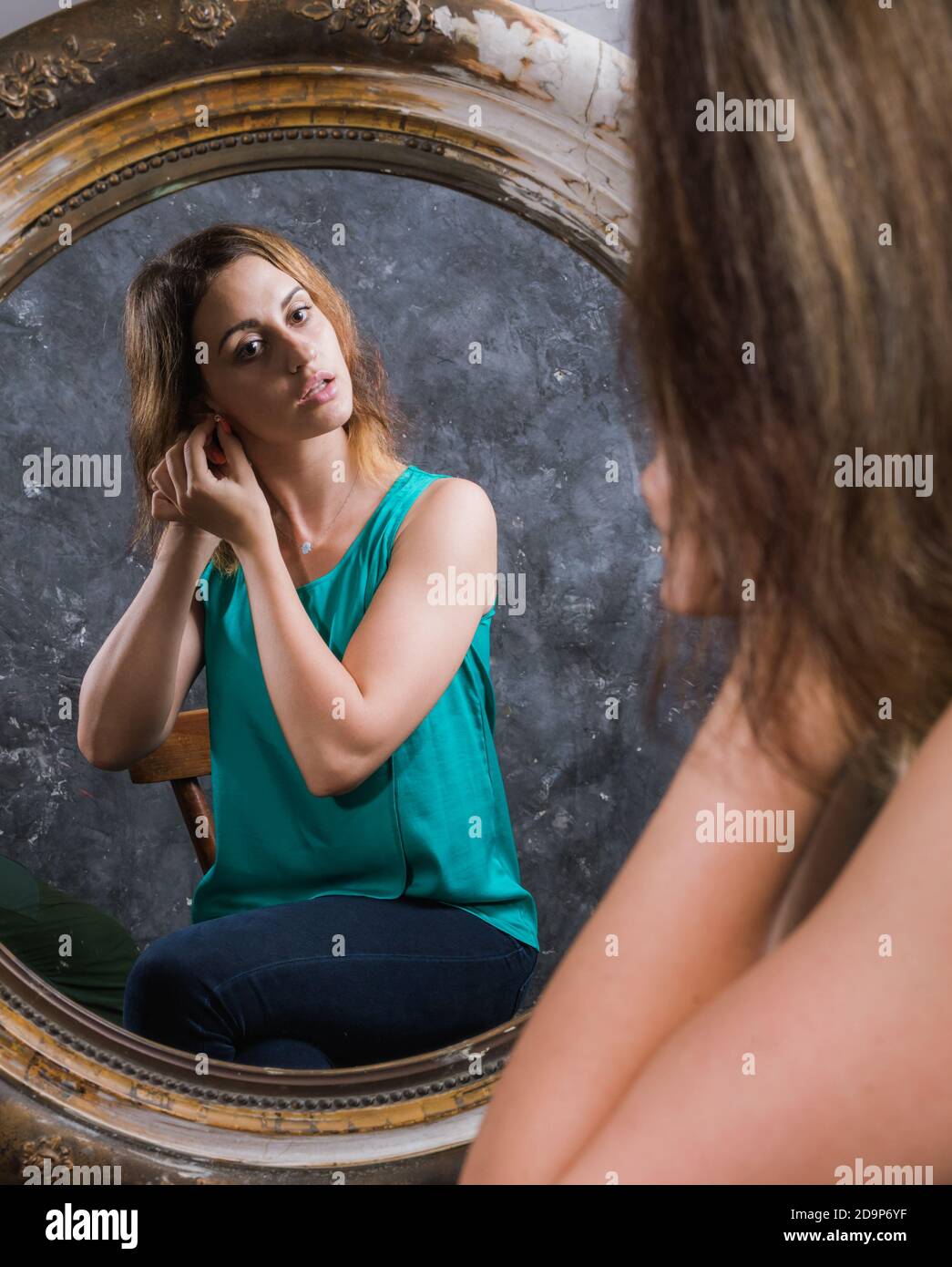 Beautiful young woman looking on her reflection at the mirror studio ...
