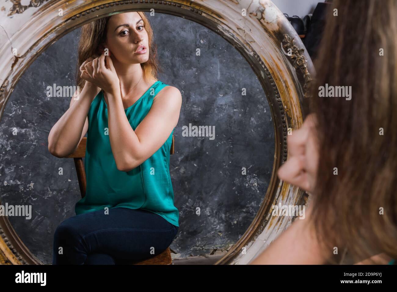 Beautiful young woman looking on her reflection at the mirror studio ...