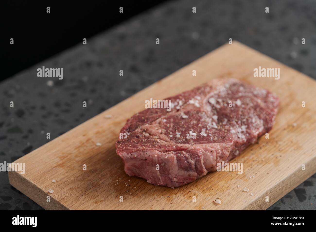Raw ribeye steak spiced and ready to cook on oak board , shallow focus ...