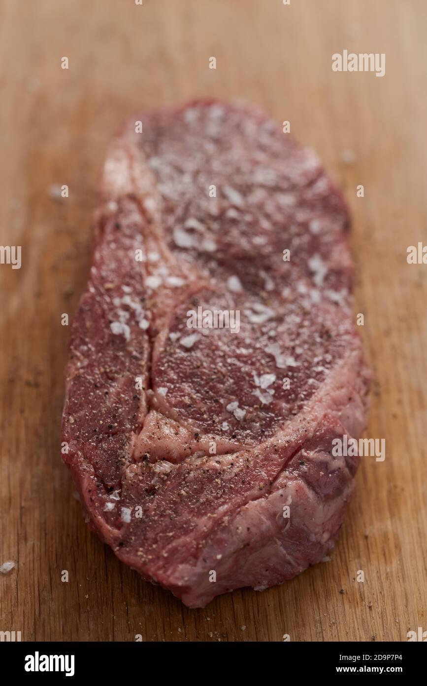 Raw ribeye steak spiced and ready to cook on oak board , shallow focus ...