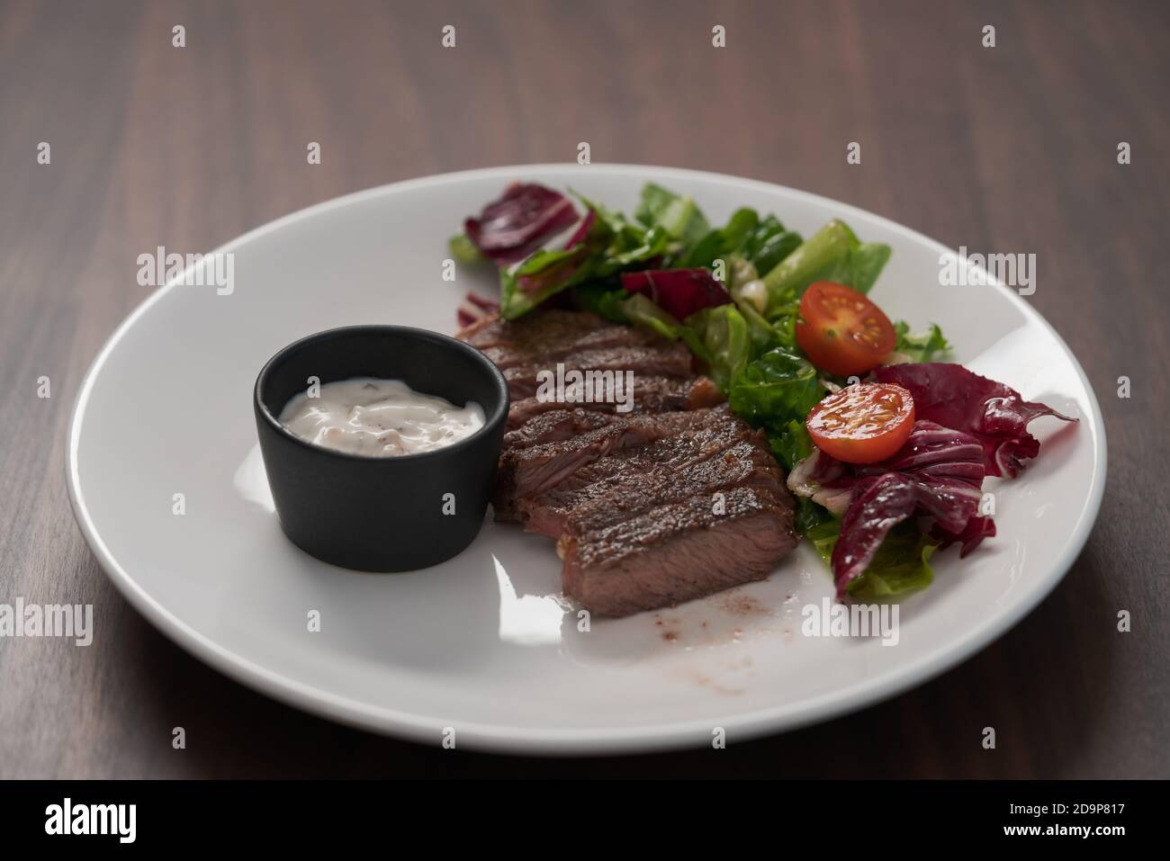 ribeye steak with garlic sauce and fresh salad on white plate on walnut ...