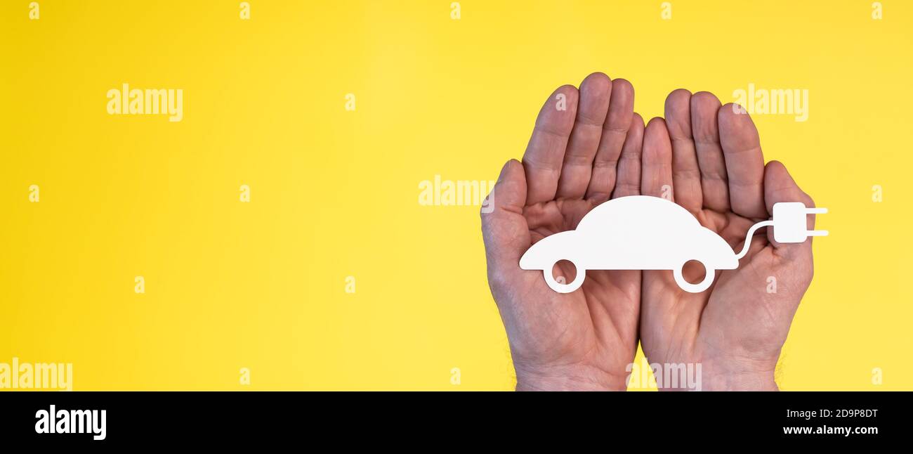 Hands holding a paper electric car on yellow background; Concept of eco ...