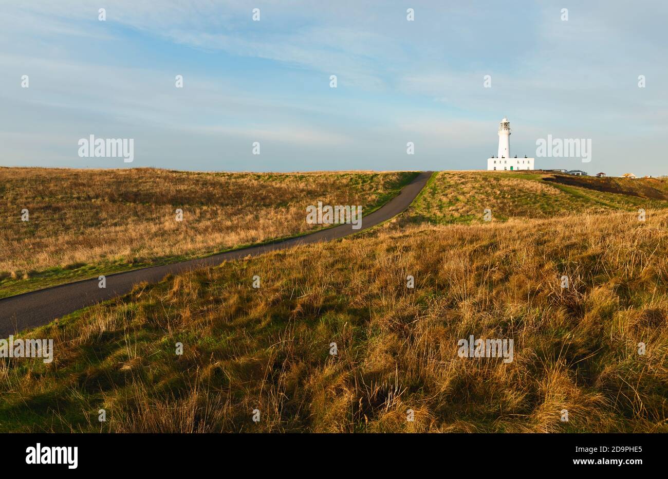 Lighthouse under blue sky with grasses and road running down the middle ...