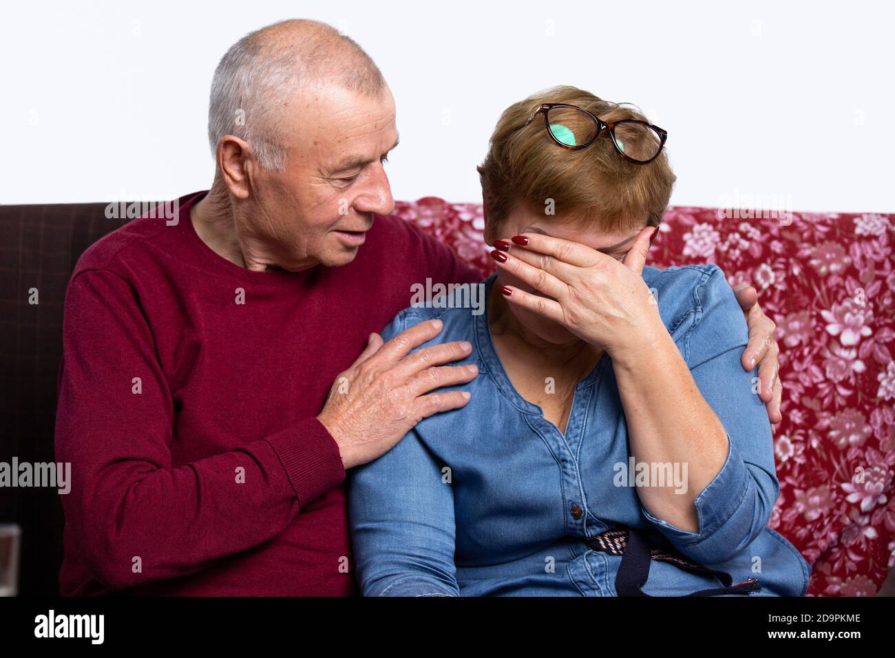 Elderly spouses are sitting on the couch at home, the wife is crying ...