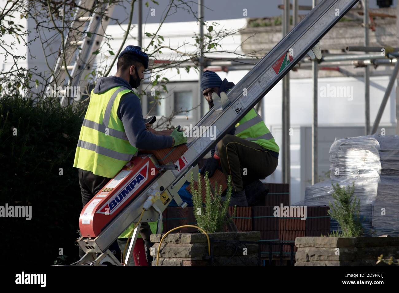 A builder with a facemark around his chin places bricks on a brick lift ...