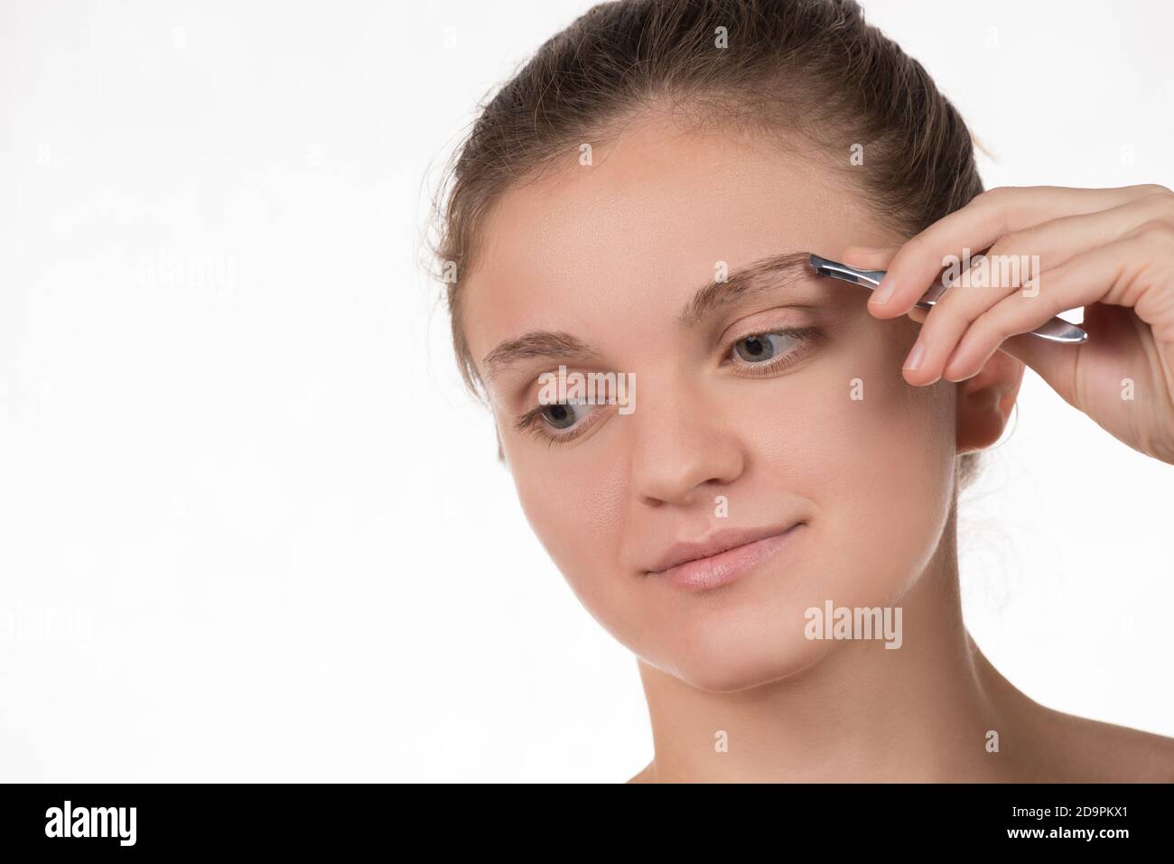 Young beautiful girl pulls out her eyebrows with tweezers metal on a ...