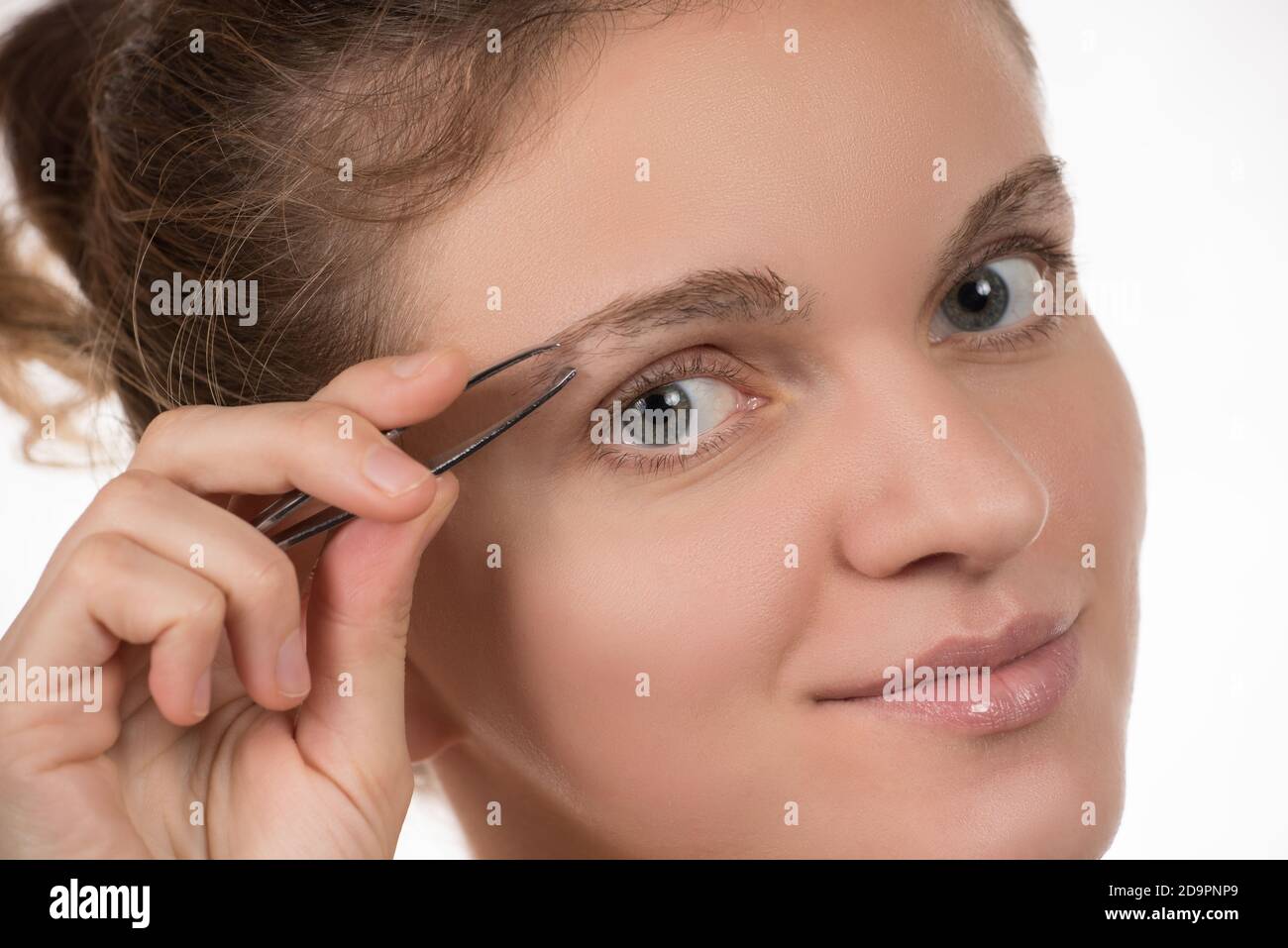 Young beautiful girl pulls out her eyebrows with tweezers metal on a ...