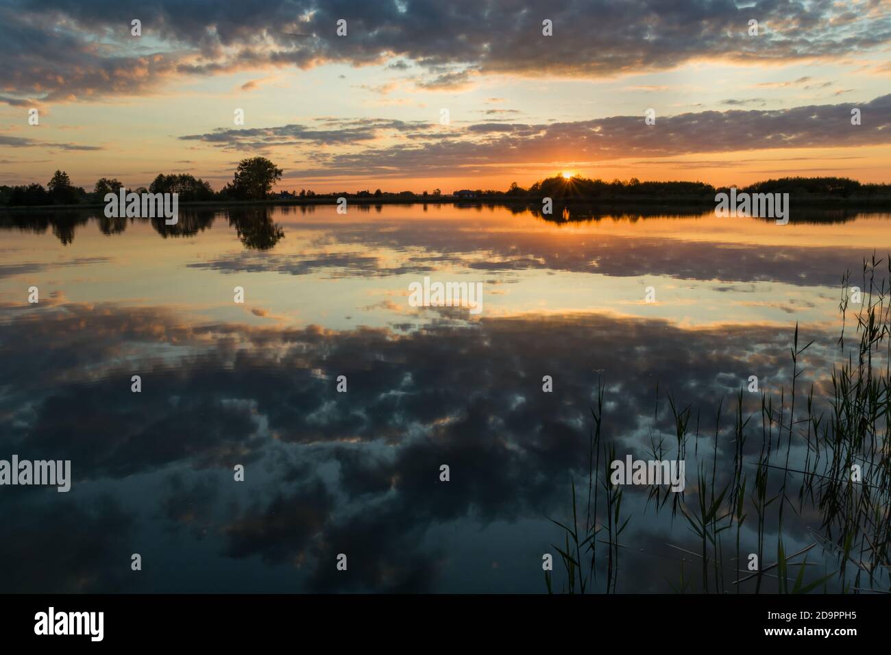 Beautiful sunset over a calm lake and reflection of clouds in the water ...