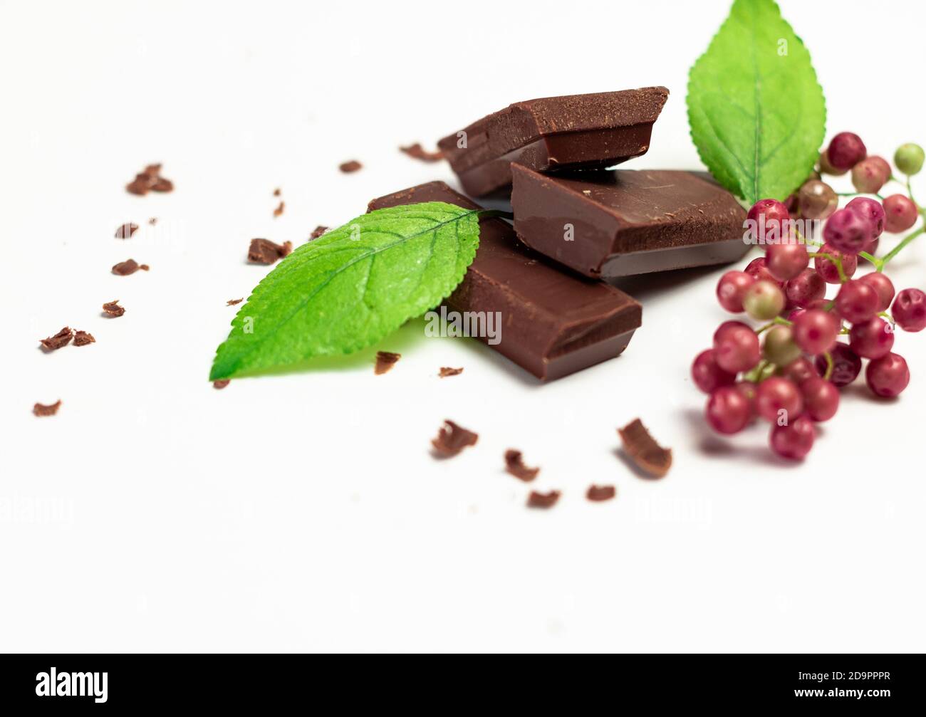 Chocolate pieces with green leaves and red berries on white background ...