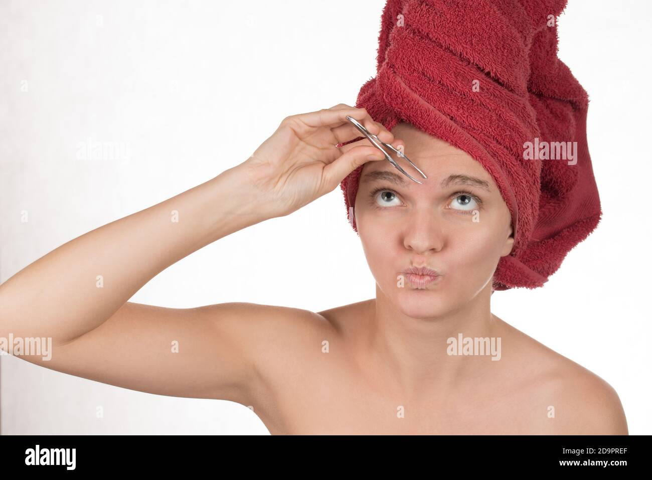 Young beautiful girl pulls out her eyebrows with tweezers metal on a ...