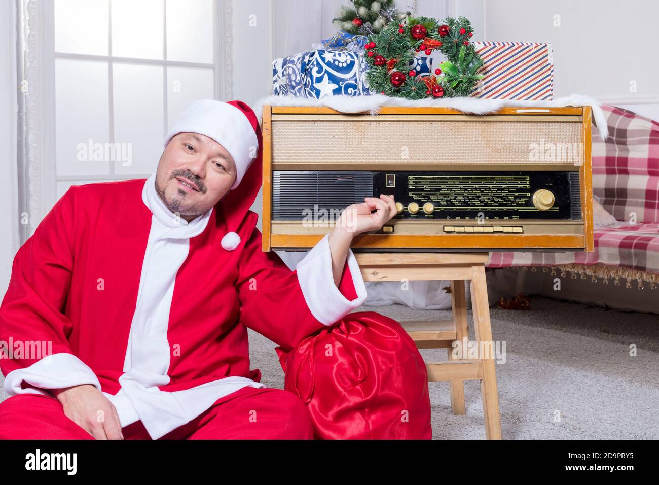 Bearded man dressed in Santa Claus costume sitting close to retro radio ...