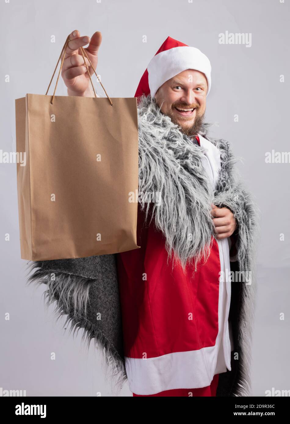 Cheerful Santa dressed in fur skin offering a present studio portrait ...