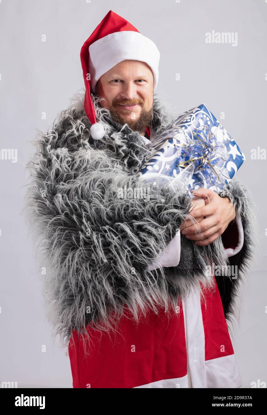 Cheerful Santa dressed in fur skin offering a present studio portrait ...
