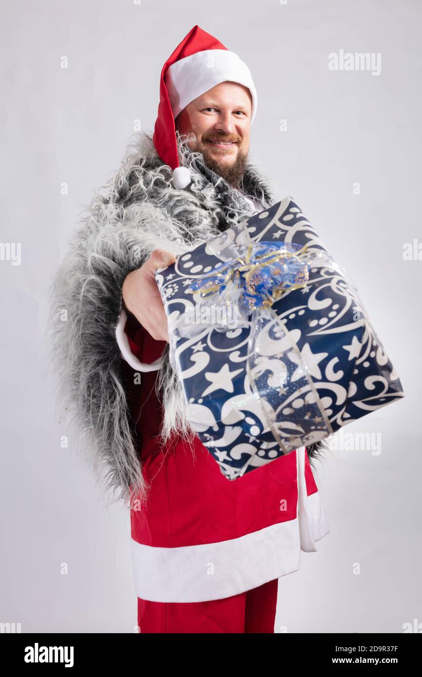 Cheerful Santa dressed in fur skin offering a present studio portrait ...