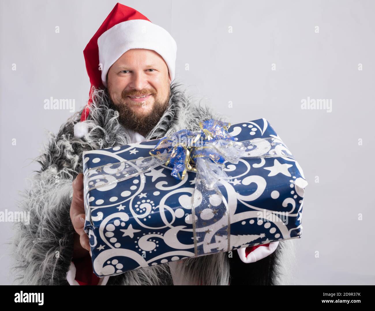 Cheerful Santa dressed in fur skin offering a present studio portrait ...