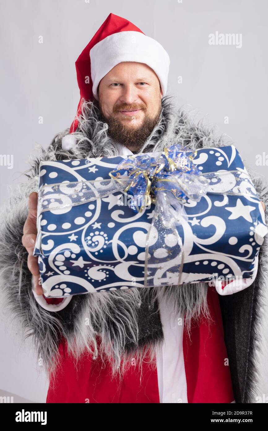 Cheerful Santa dressed in fur skin offering a present studio portrait ...