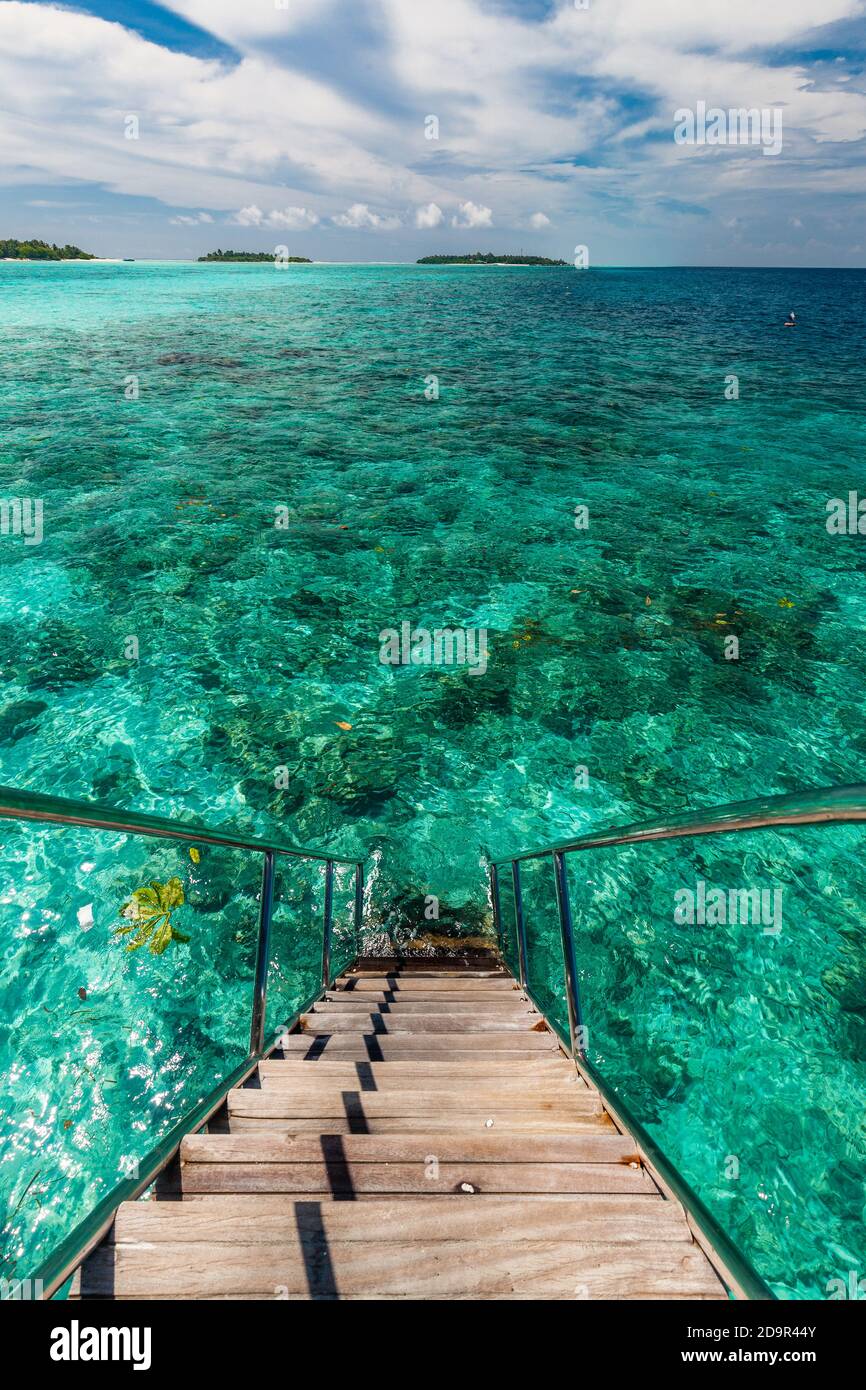 Jetty over swimming atoll and a tropical resort island in Maldives ...